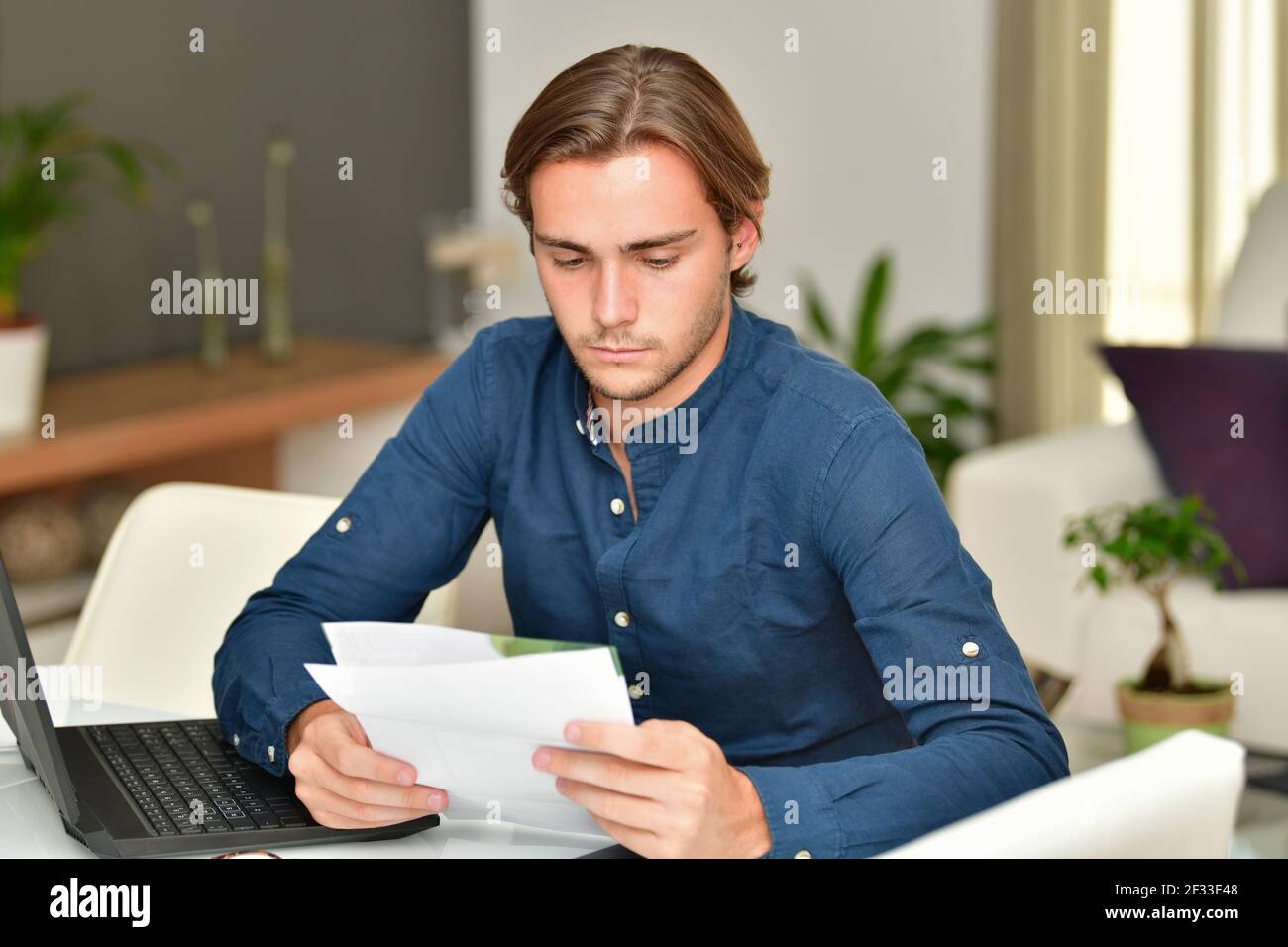 Handsome young man looking closely at some bills while sitting next to ...