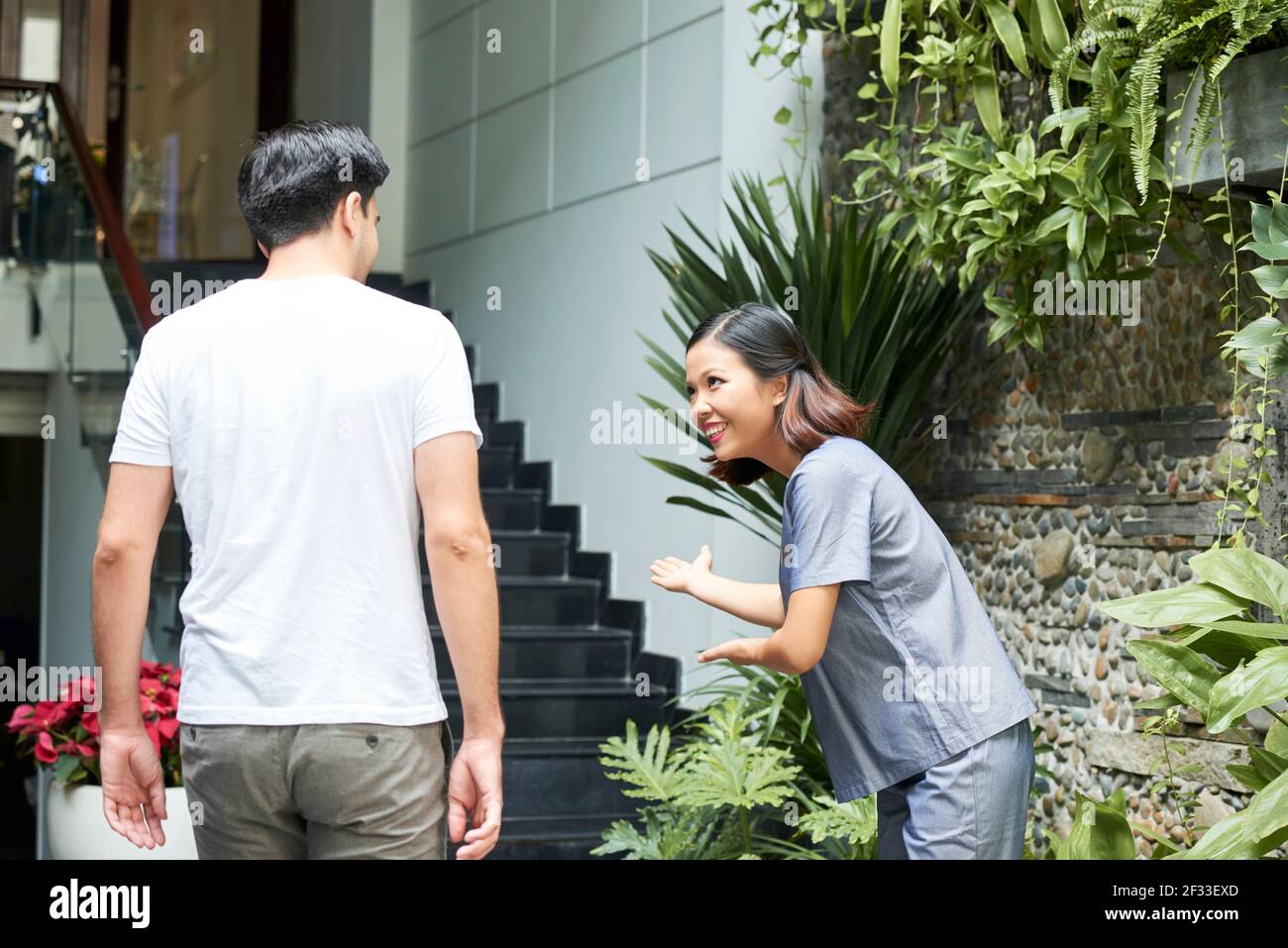 Smiling pretty Asian woman bowing to man entering spa salon building ...