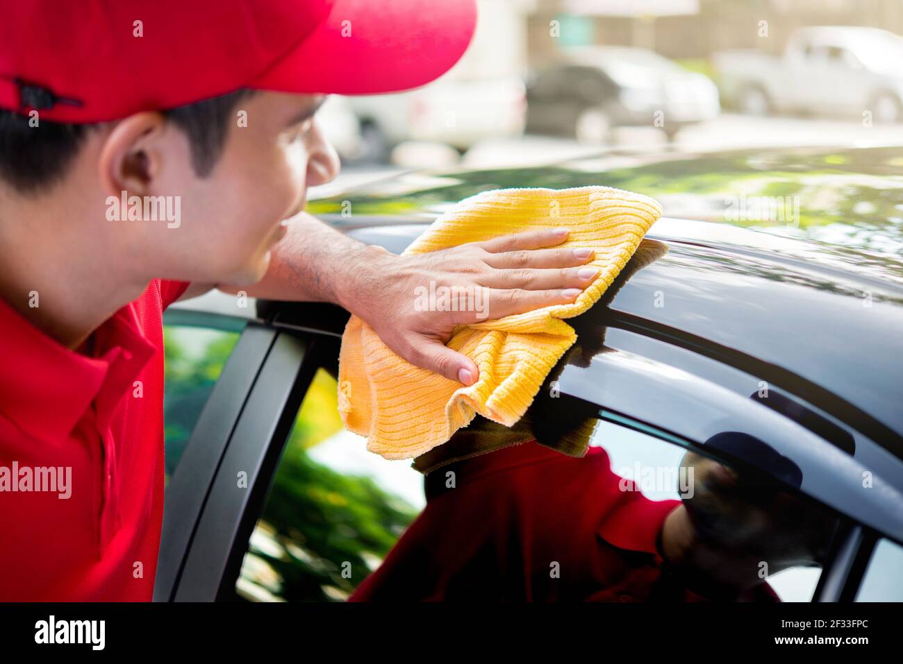 Auto service staff in red uniform cleaning car with microfiber cloth ...
