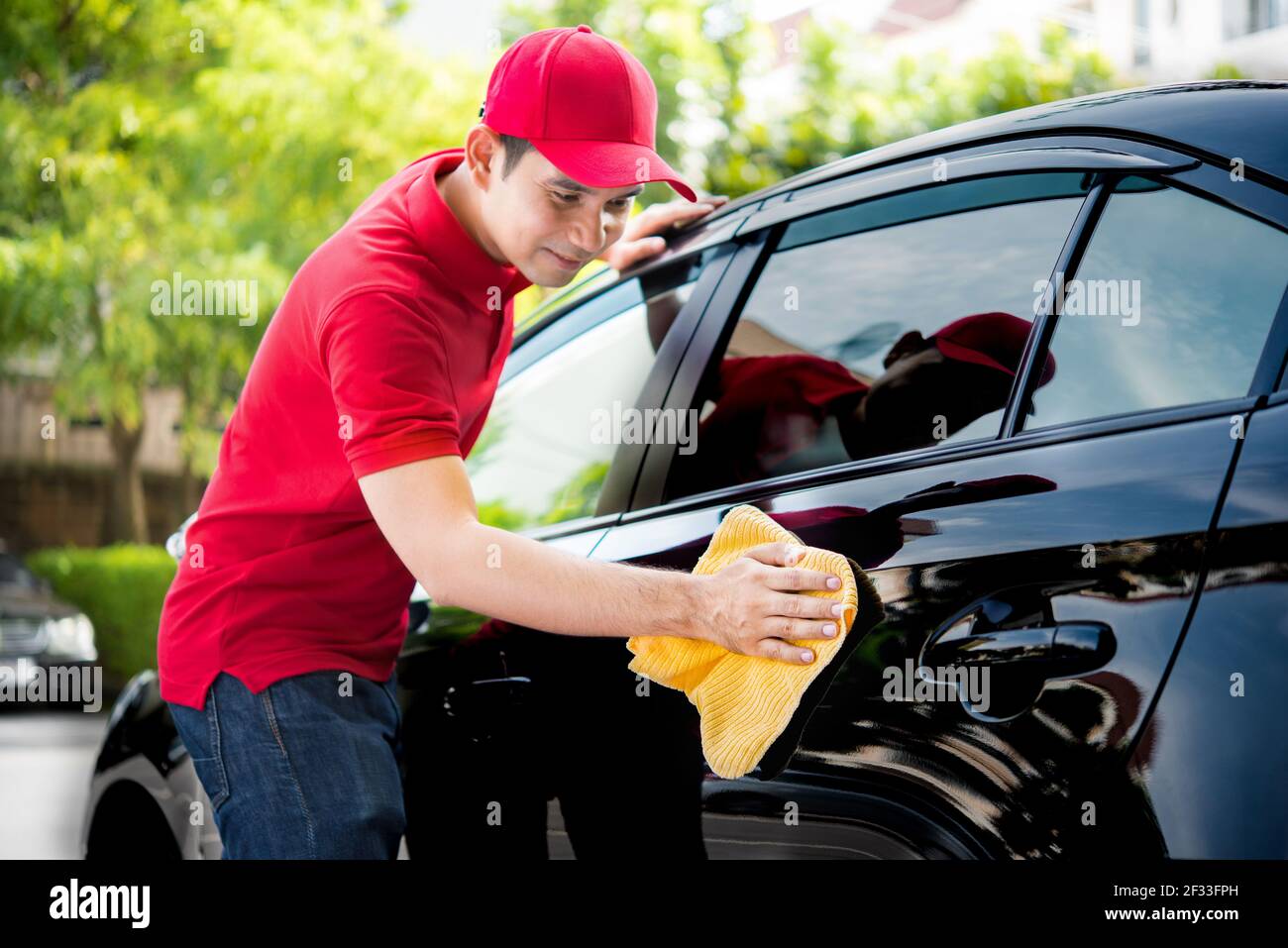 Auto service staff in red uniform cleaning car with microfiber cloth ...