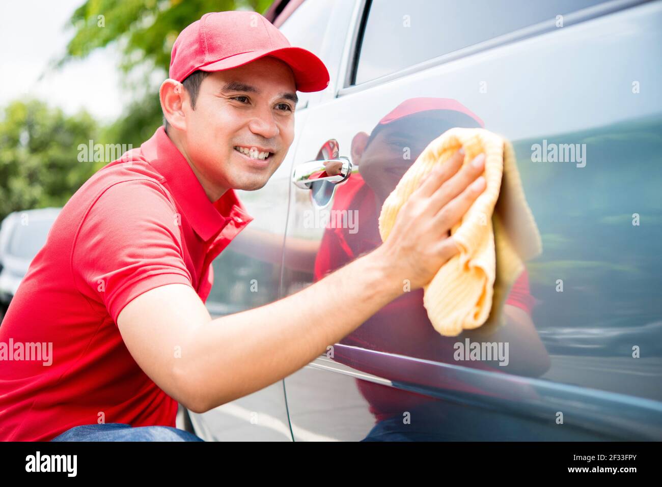 Auto service staff in red uniform cleaning car with microfiber cloth ...