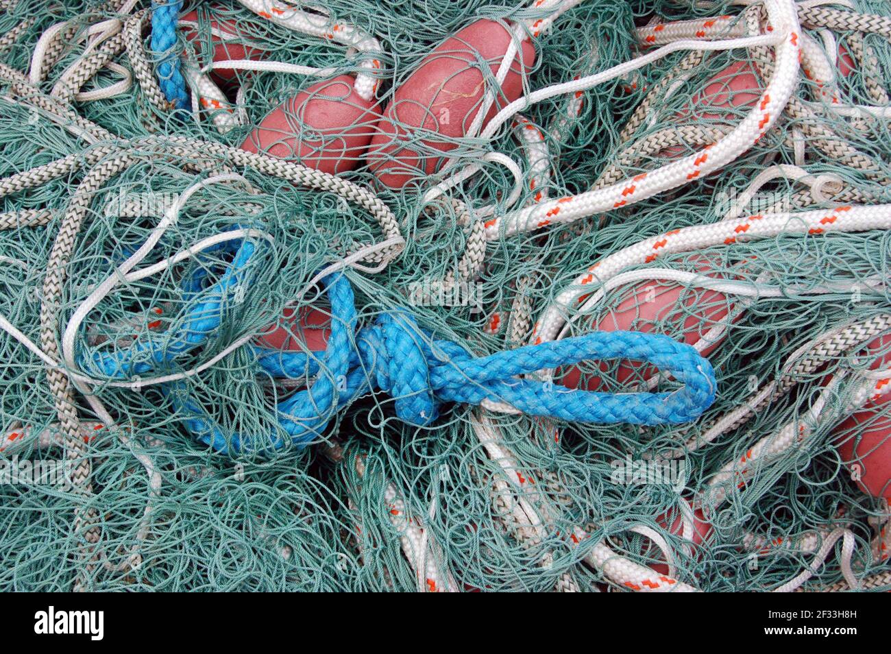 A messy pile of fishing net, ropes and floats drying in the sunshine at ...