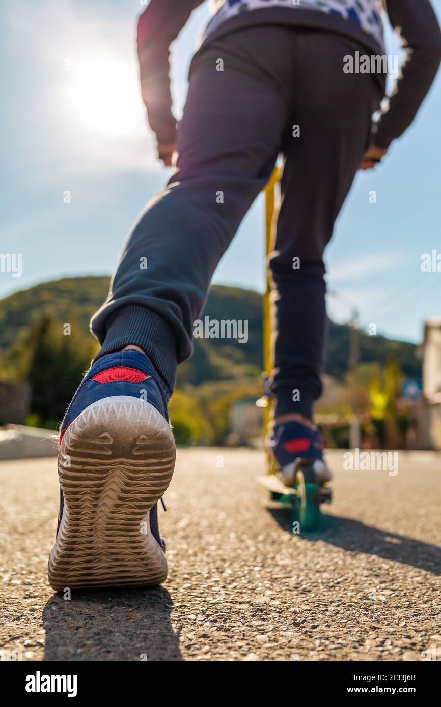 A teenage boy rides a scooter, pushing off with his left foot. Legs ...