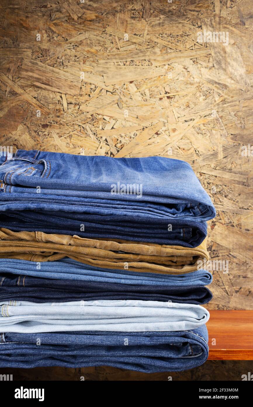 Denim jeans at wooden shelf near aged chipboard wall background texture ...