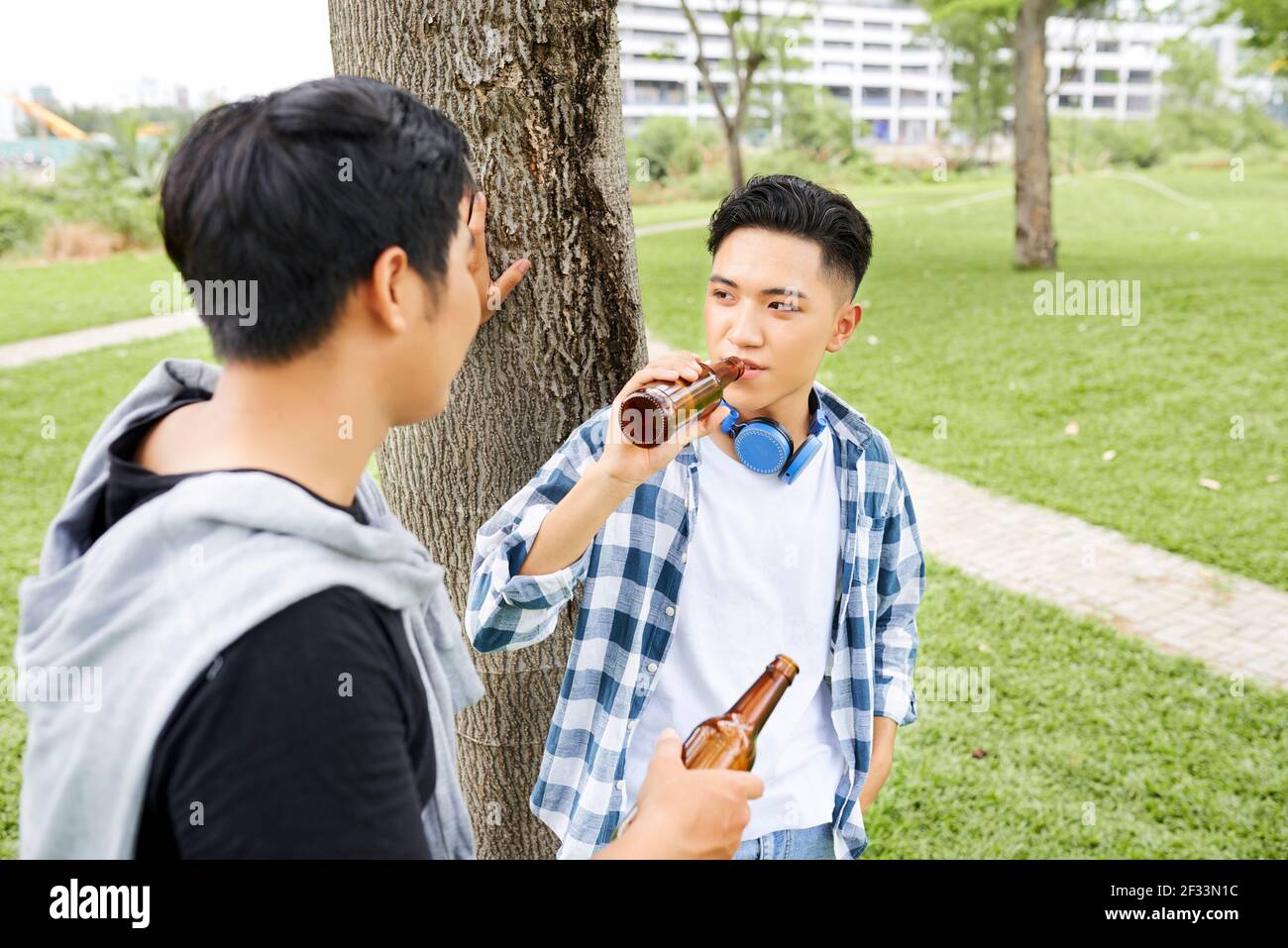 Two teenage boys drinking beer from bottles together while standing ...