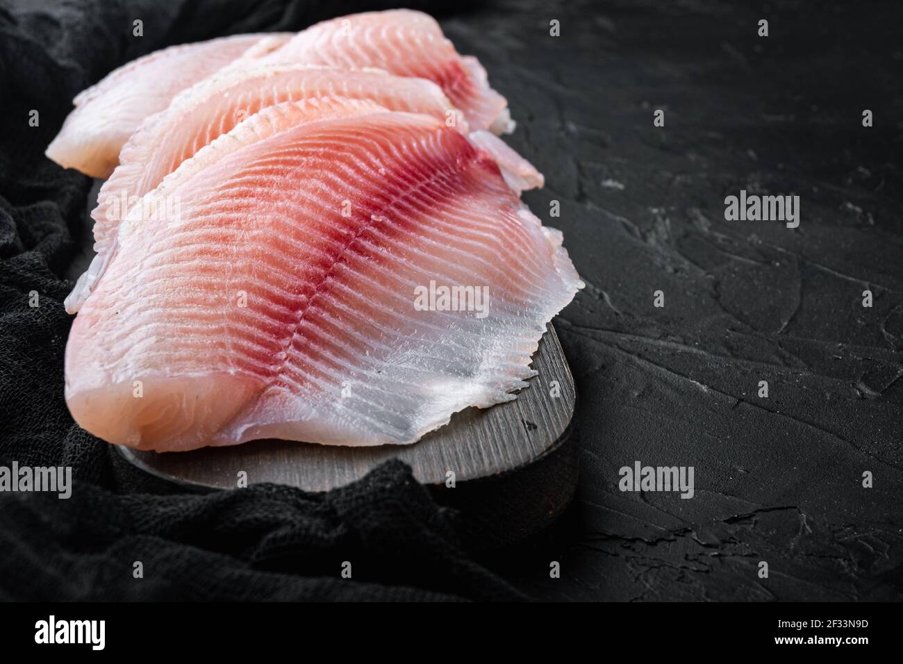 Tilapia fish, skinless meat, on black background Stock Photo - Alamy