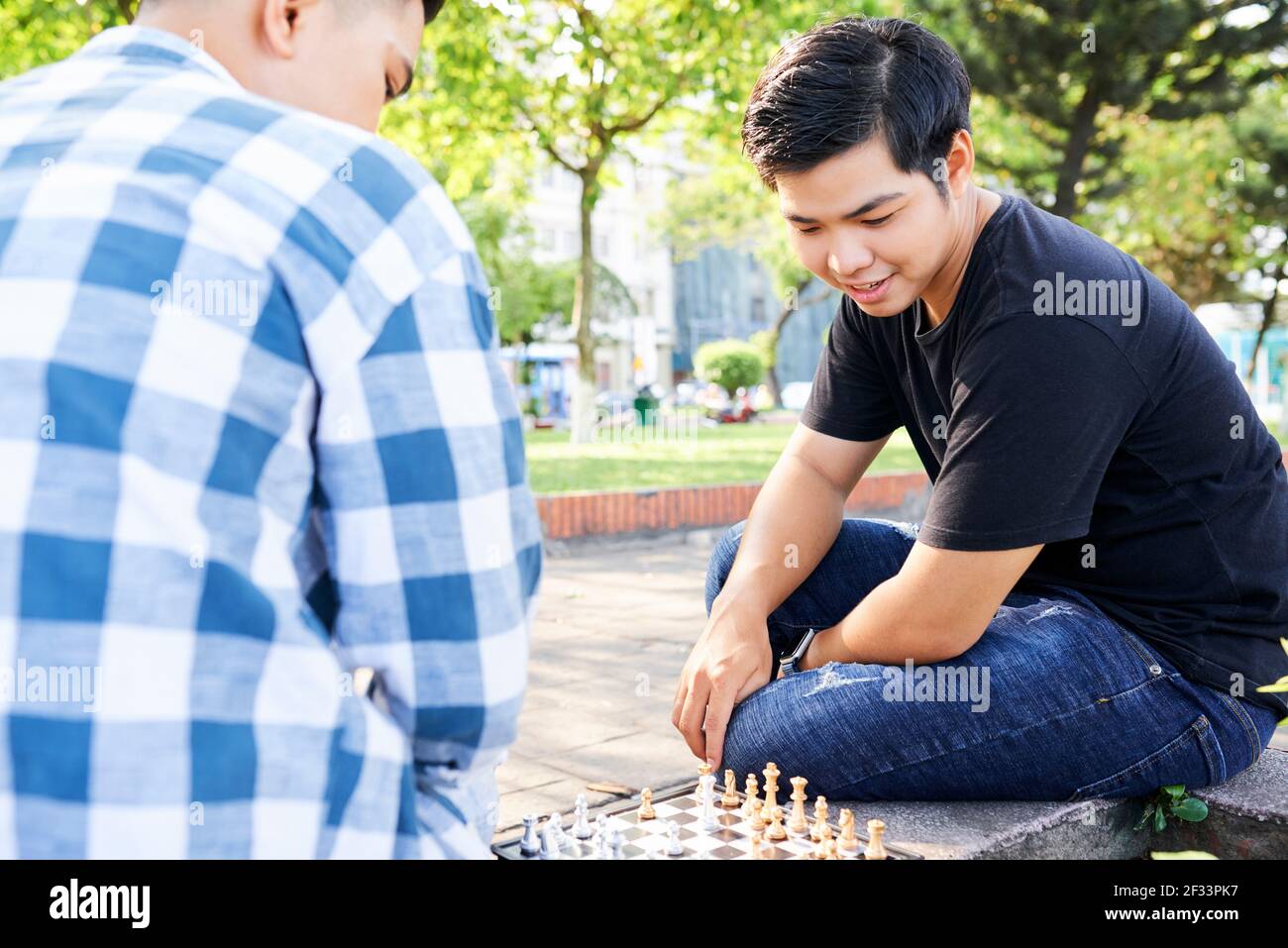 Two Asian guys sitting on bench on the street and playing chess ...