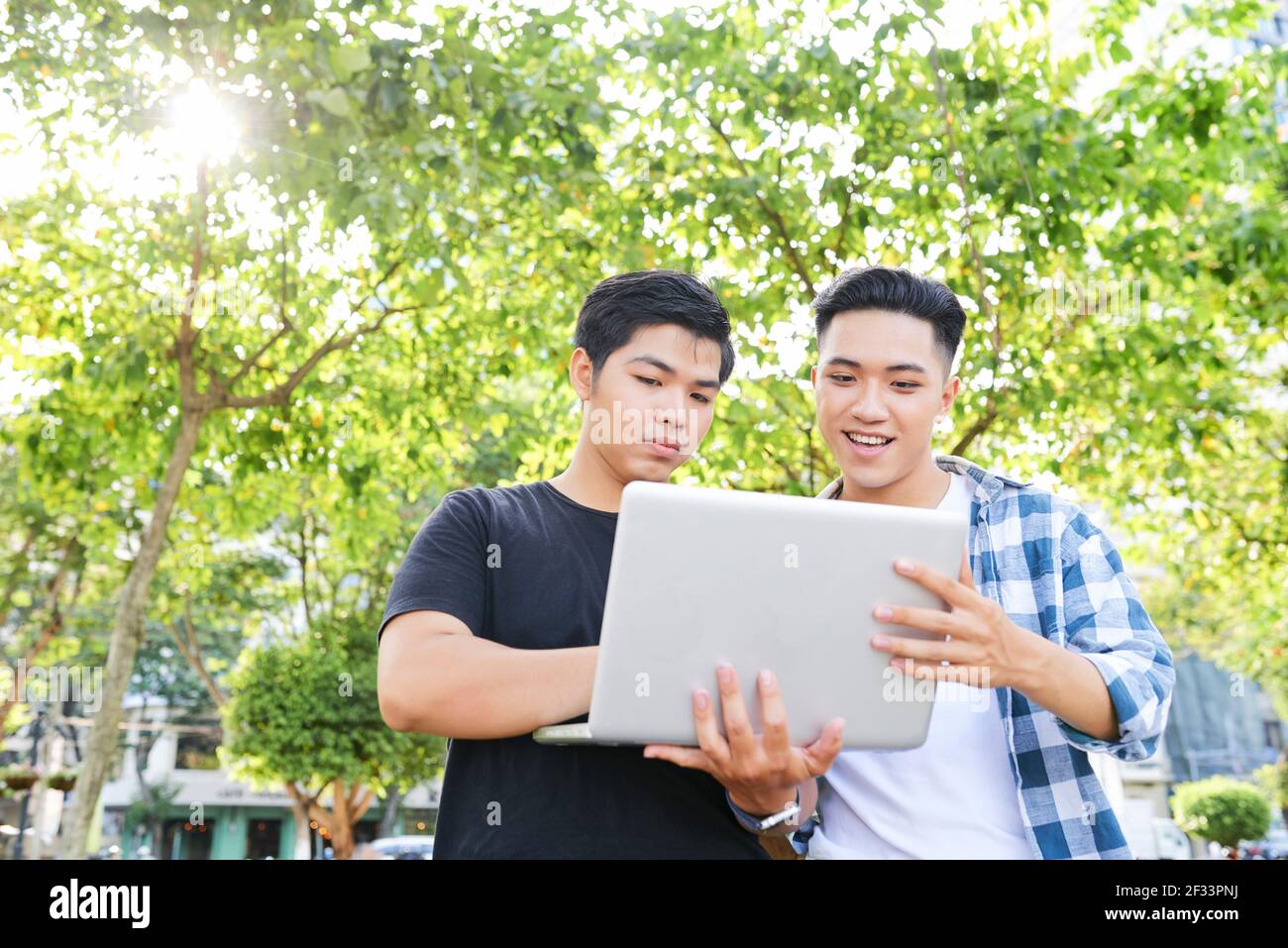 Two Asian men holding laptop and using it together in the city outdoors ...