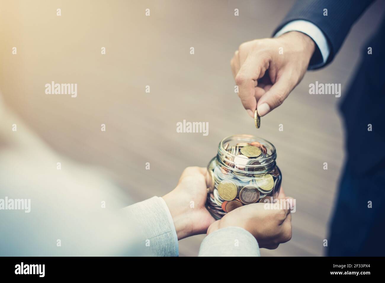 Businessman hand putting money (coin) in the glass jar held by a woman ...