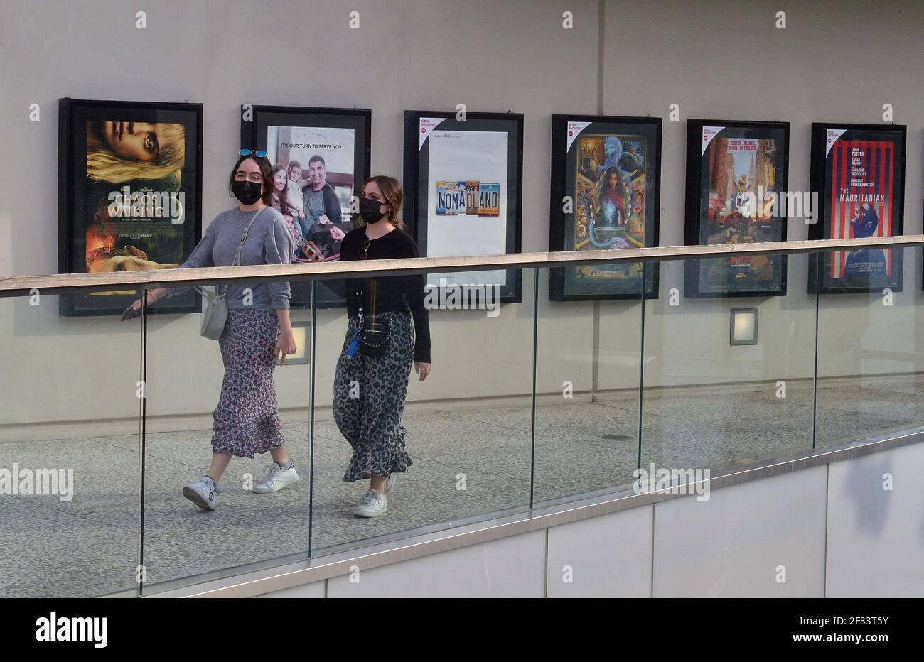 Two women walk past posters of recently released movies at the AMC ...