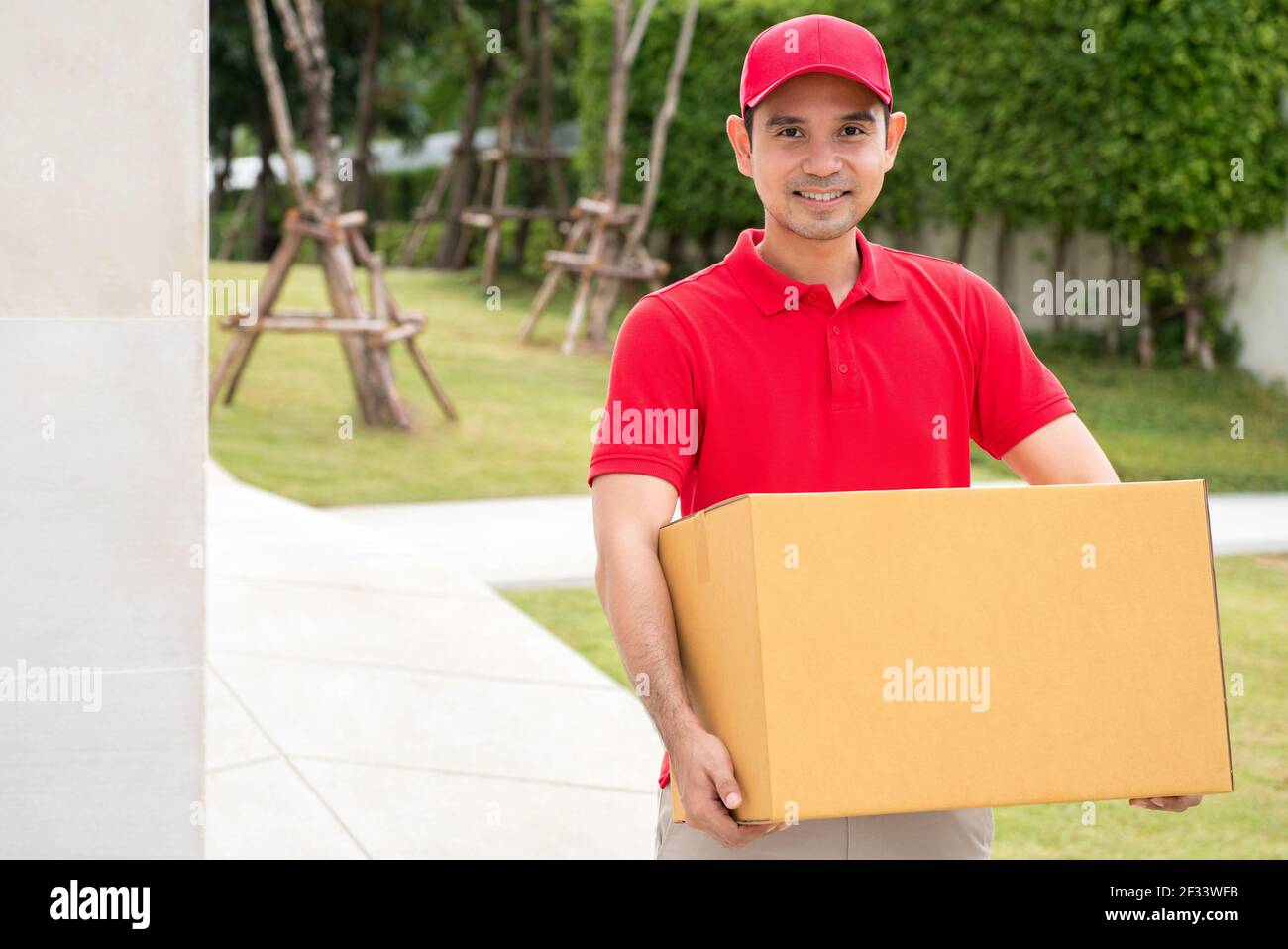 Delivery man in red uniform holding parcel box Stock Photo - Alamy