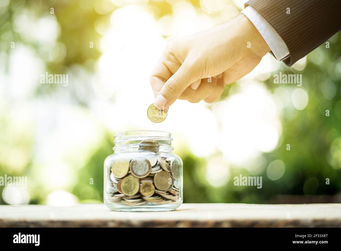 Businessman hand putting money (coin) into the glass jar - savings ...