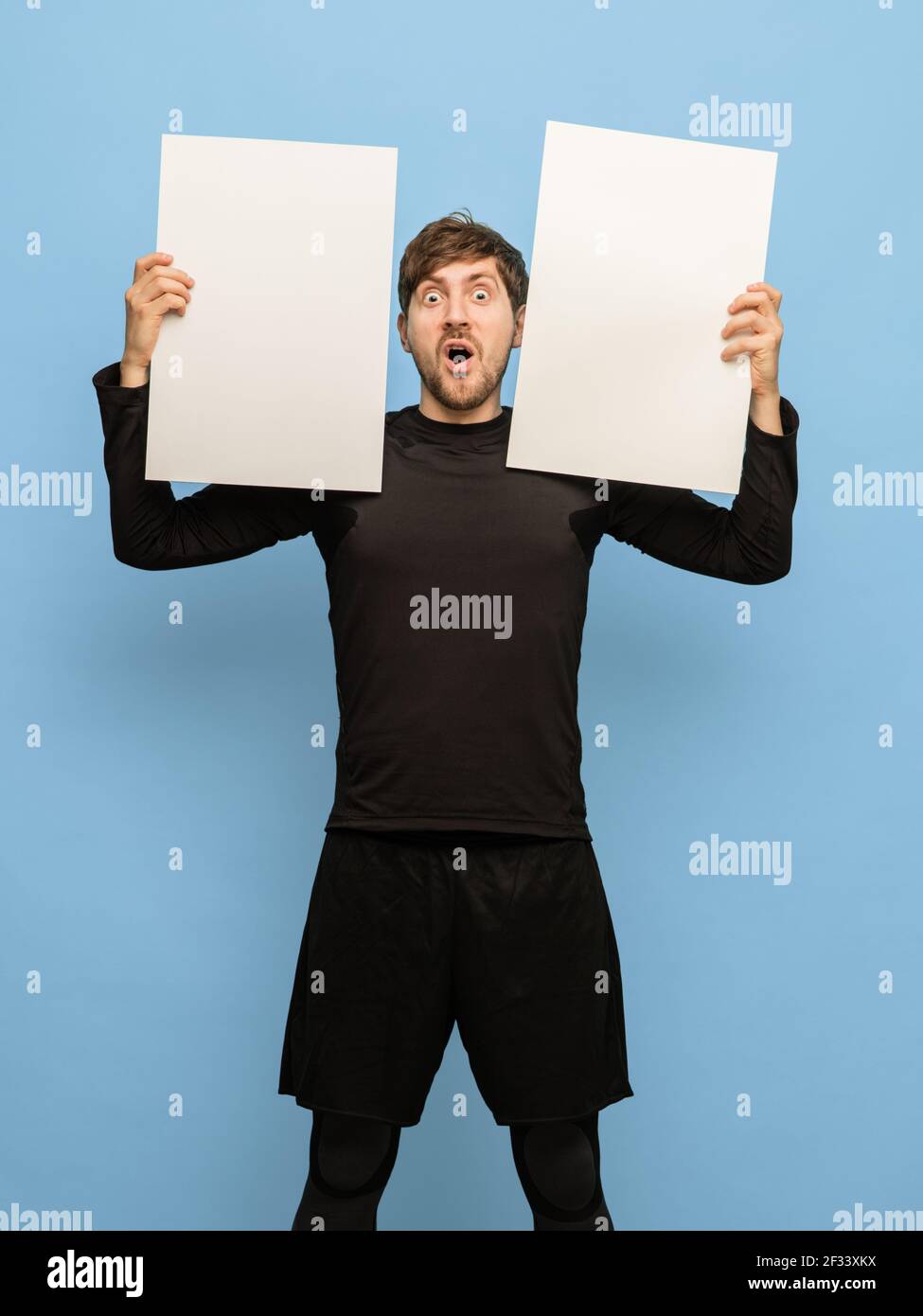 Young shocked man in black attire with blank sheet of paper on blue ...