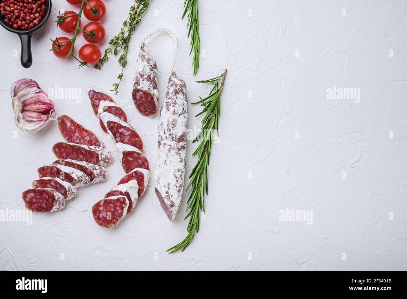 Dry cured fuet salami sausage slices with herbs on white surface, top ...