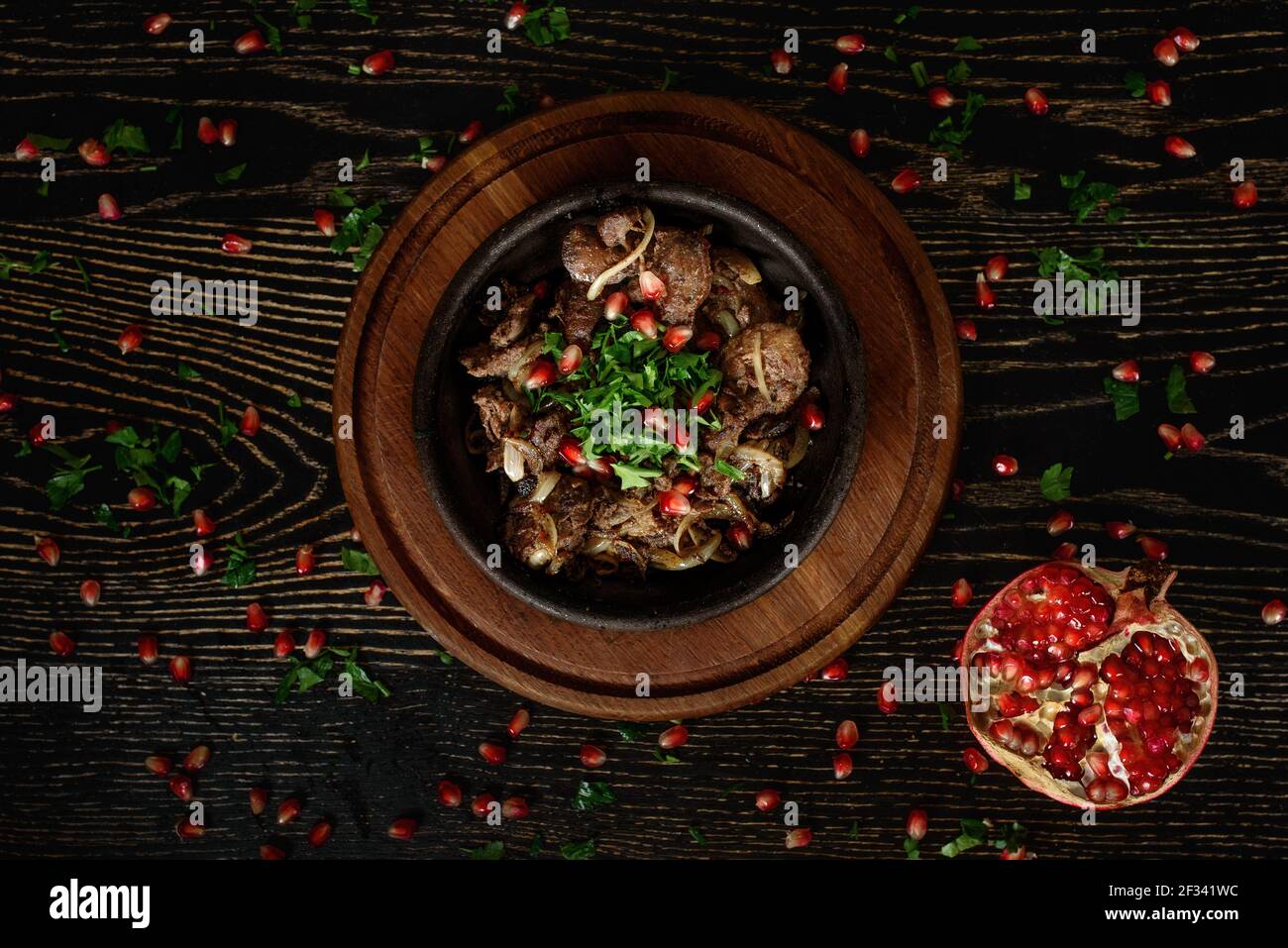 Barbecue meat with onions in a clay plate on a wooden board on a dark ...