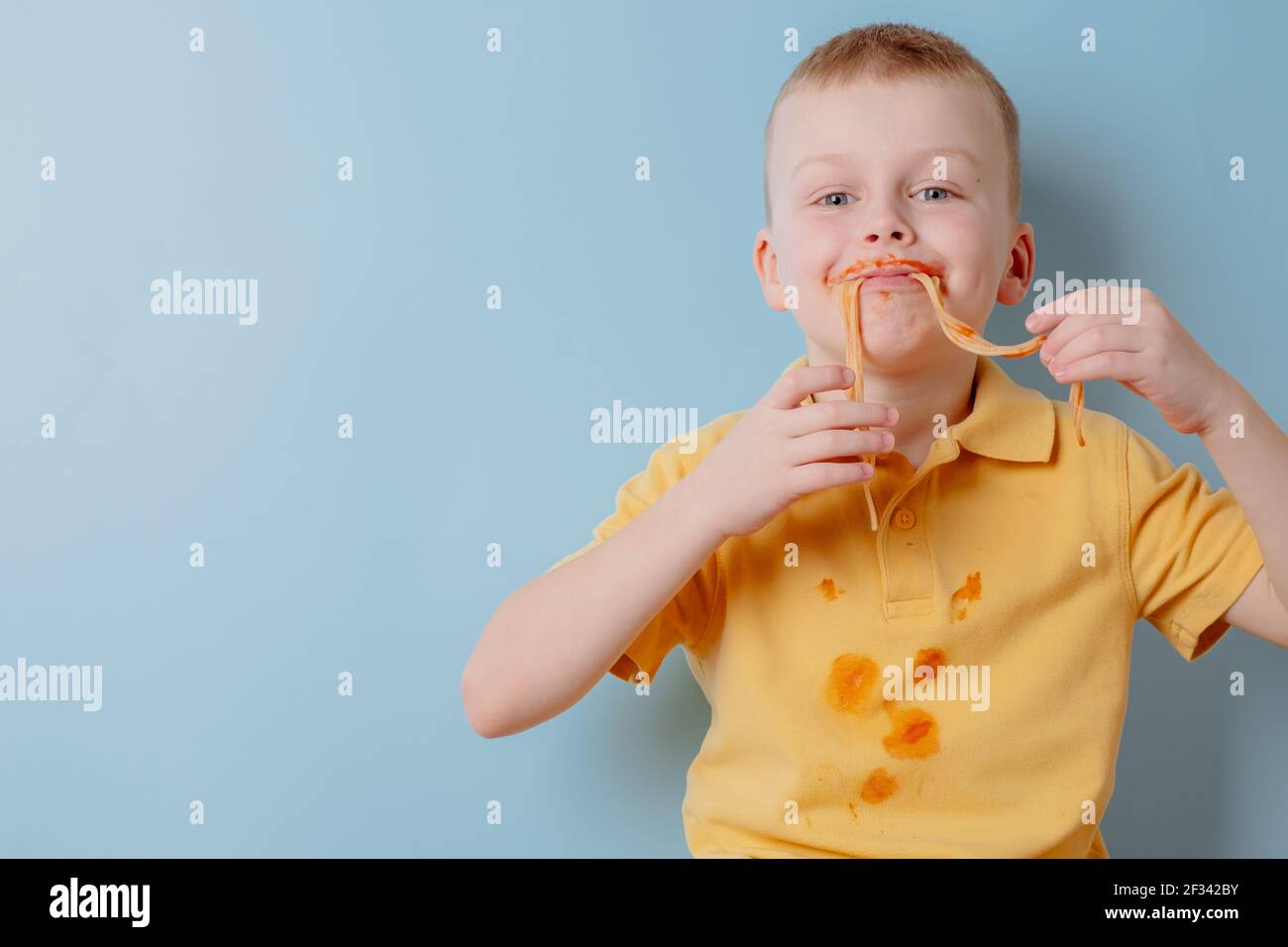 Portrait of a child eating spaghetti with hands. Boy stained with ...
