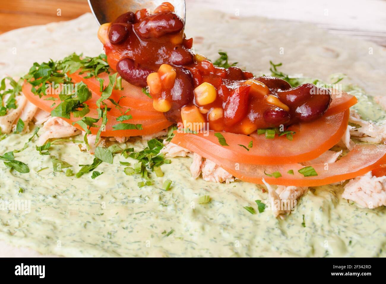 Burrito making process. The cook adds beans and corn in tomato sauce to ...