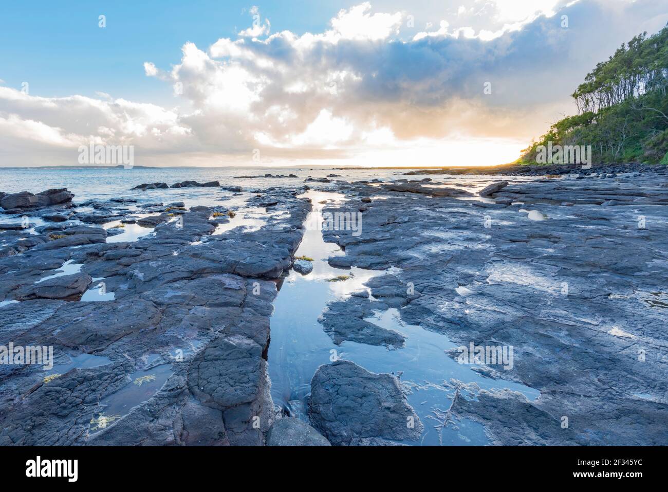 At sunrise, seawater flows in across a basalt rock shelf as the tide ...