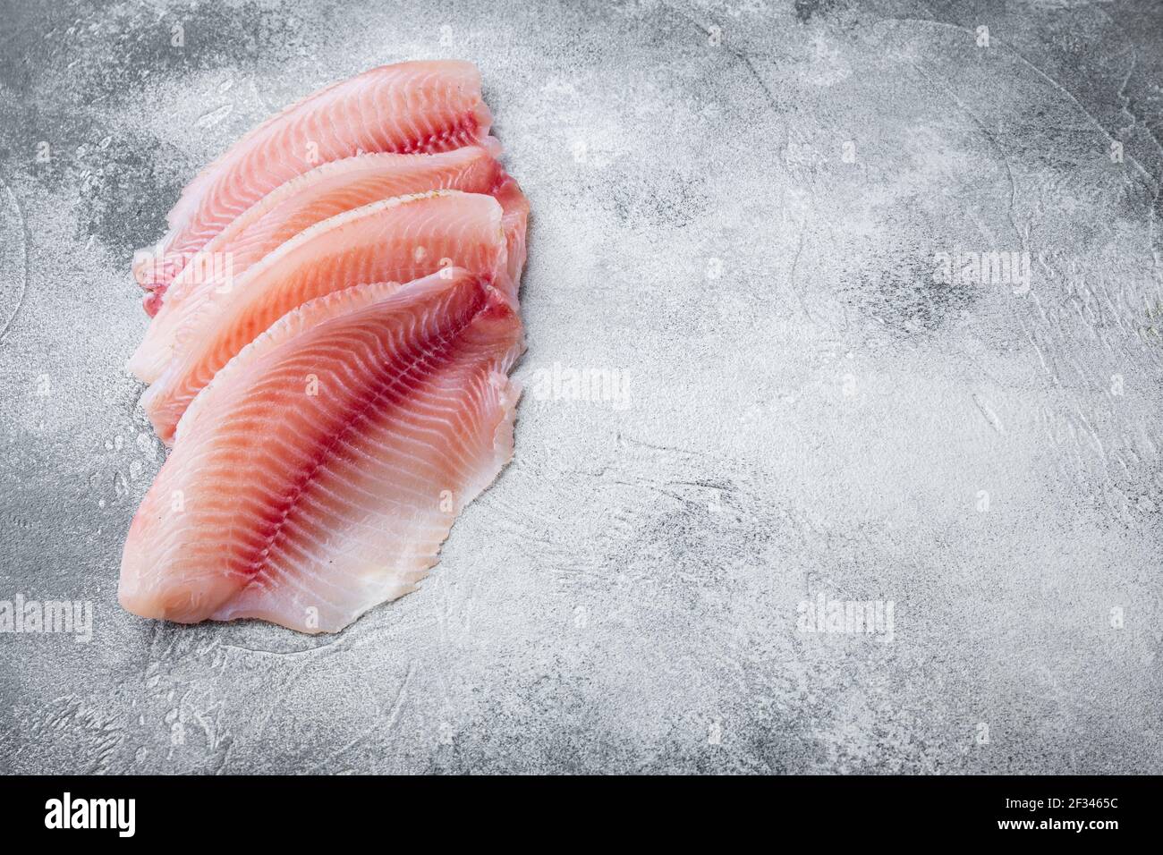 Raw tilapia fish fillet meat cuts, on gray background with copy space ...