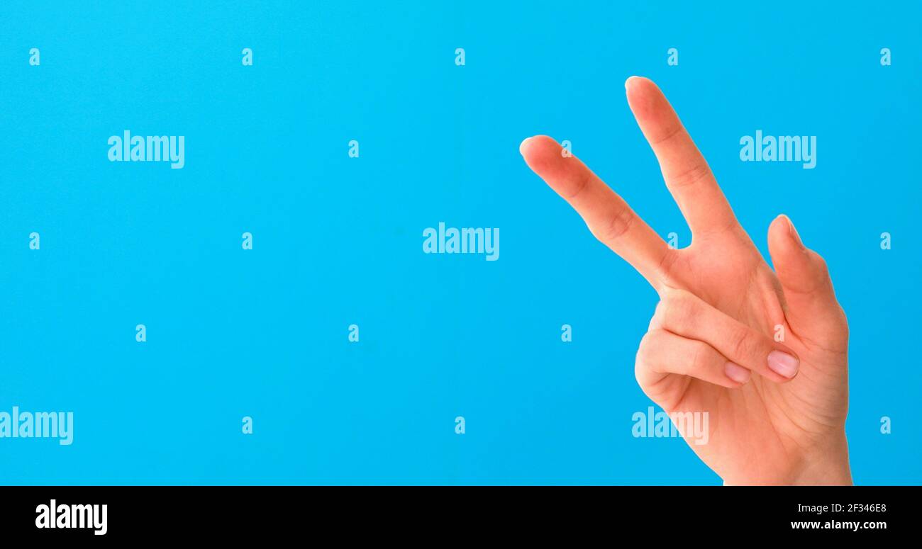 Close up of beautiful female hand doing victory sign, isolated on blue ...