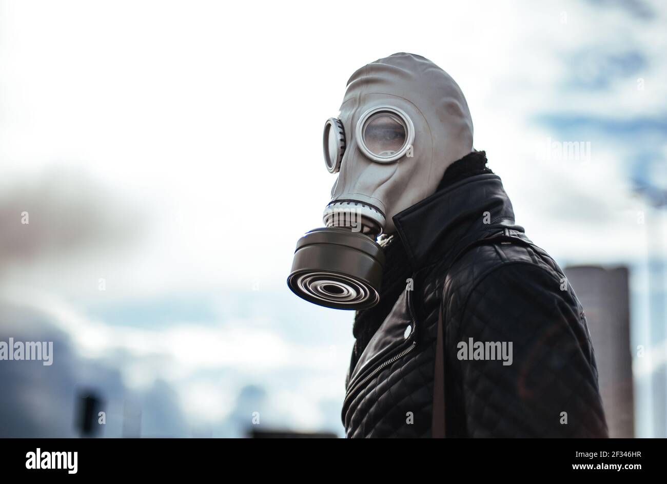 casual young man in a gas mask standing on the street in an empty city ...