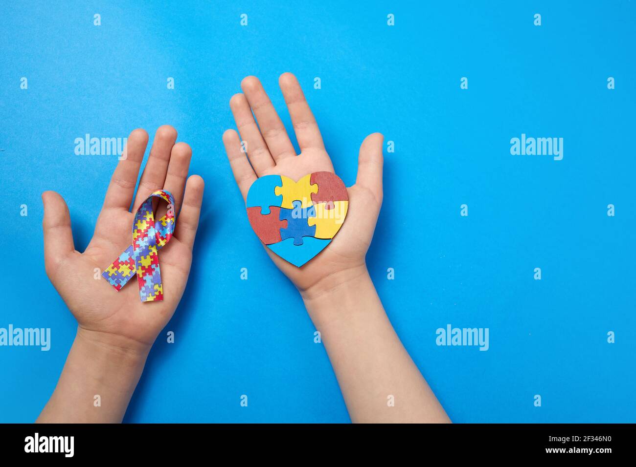 Adult and autistic boy hands holding puzzle heart shape and ribbon ...