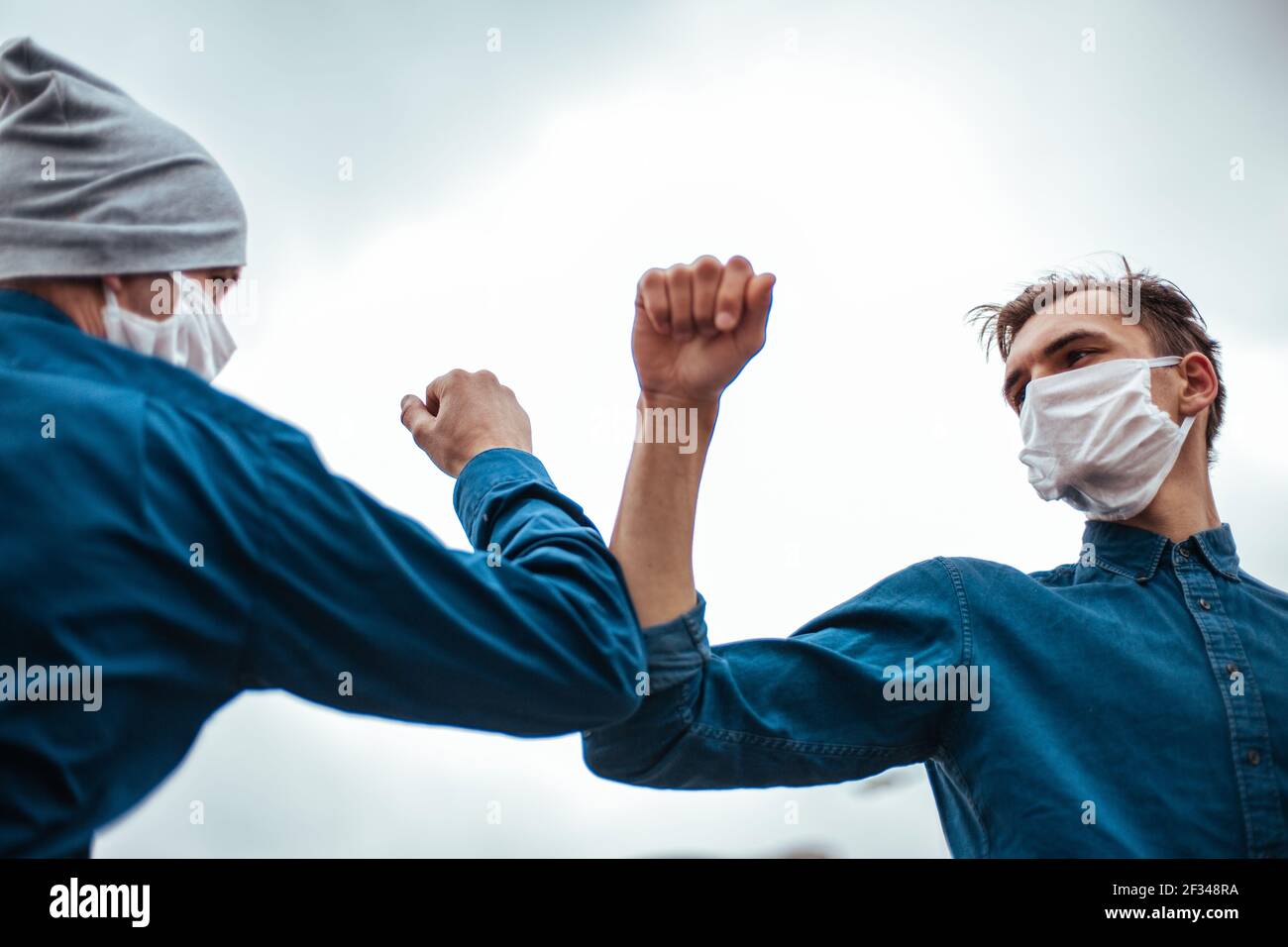 two friends greeting each other with their elbows on a city street ...