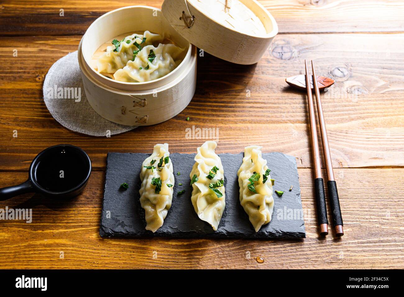 Asian dumplings on stone slate and in wooden steamer over traditional ...