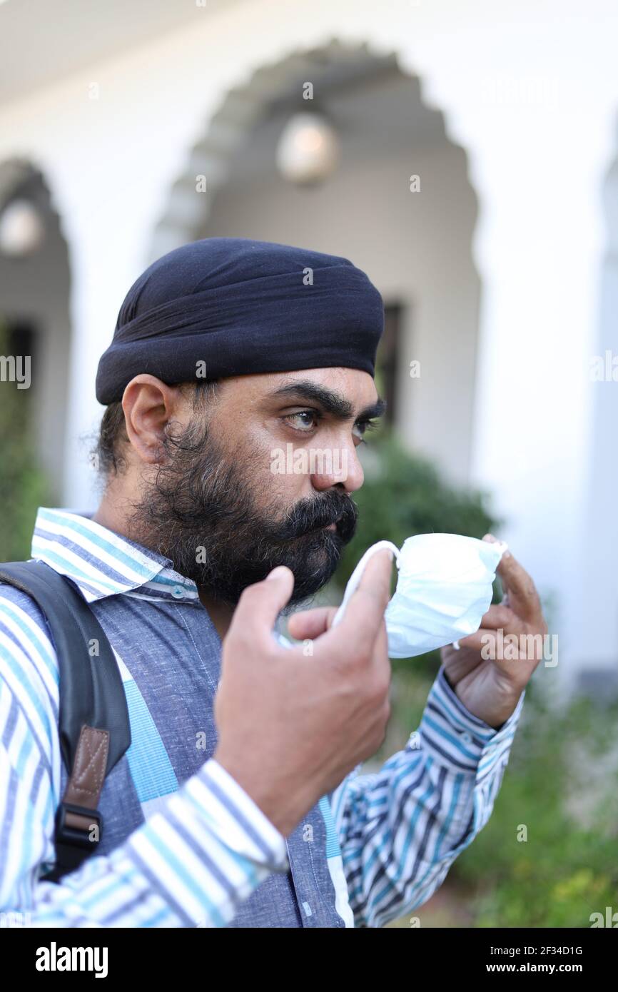 A middle-aged Indian man with a turban in the process of wearing a mask ...