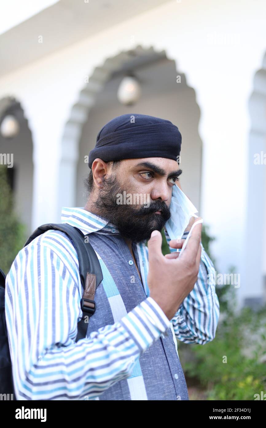 A middle-aged Indian man with a turban in the process of wearing a mask ...