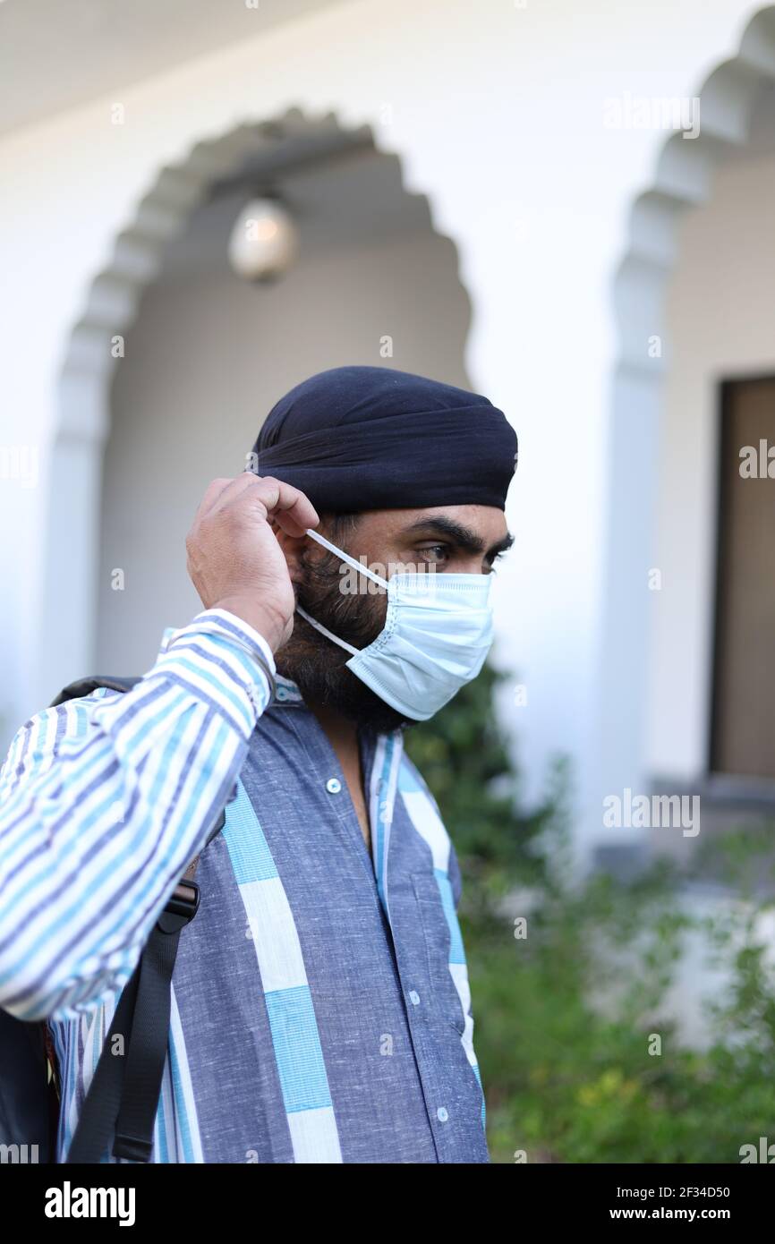 A middle-aged Indian man with a turban in the process of wearing a mask ...