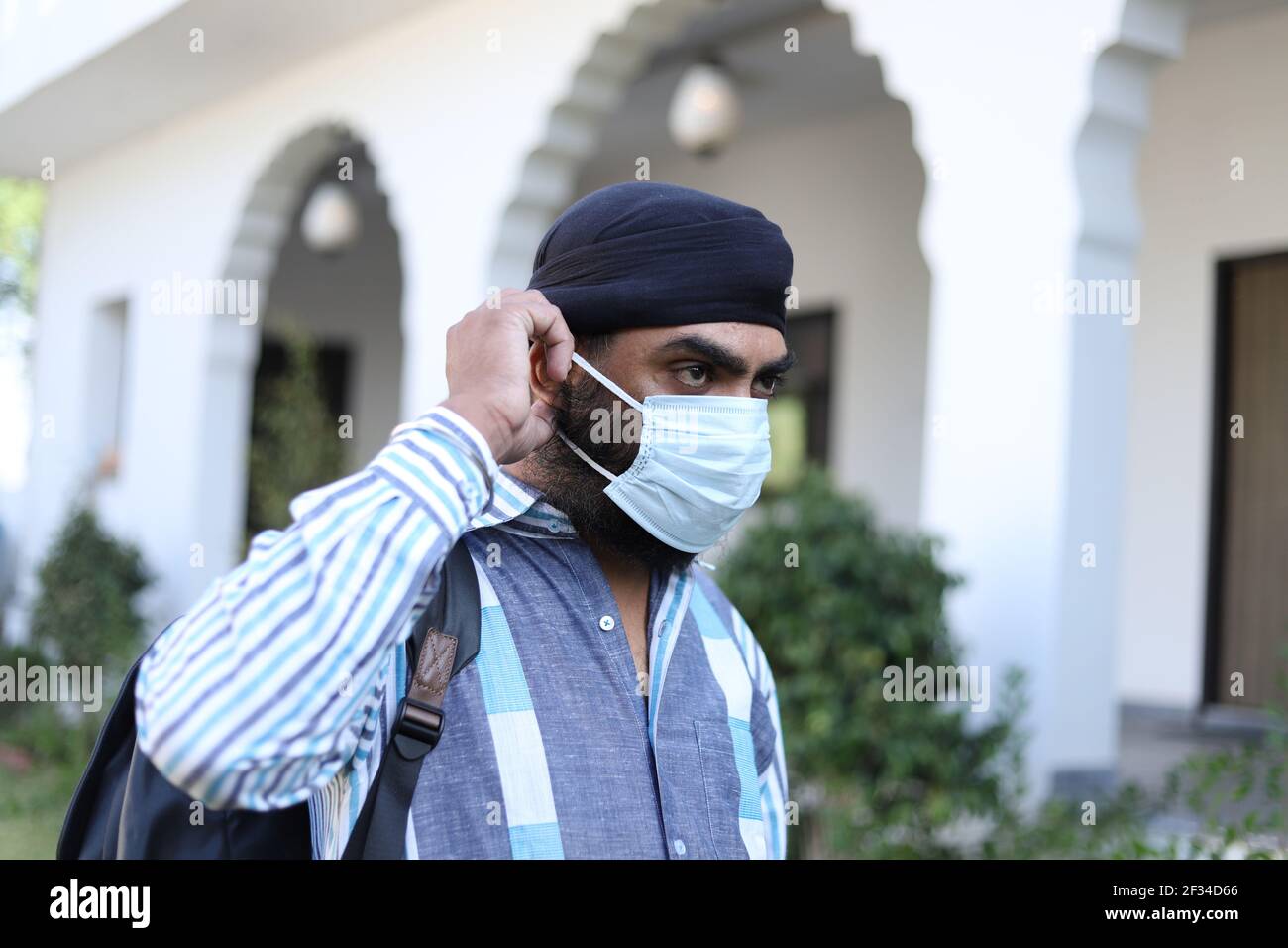 A middle-aged Indian man with a turban in the process of wearing a mask ...