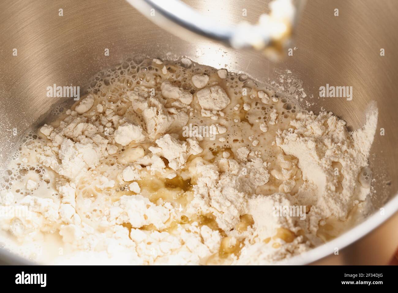 Raw yeast dough mixing in large metal bowl in mixer. Flour, water and ...