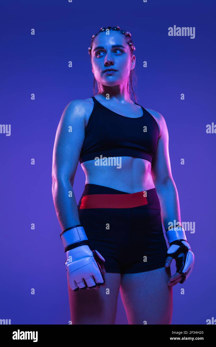 Athletic female MMA fighter posing isolated on blue background in neon ...