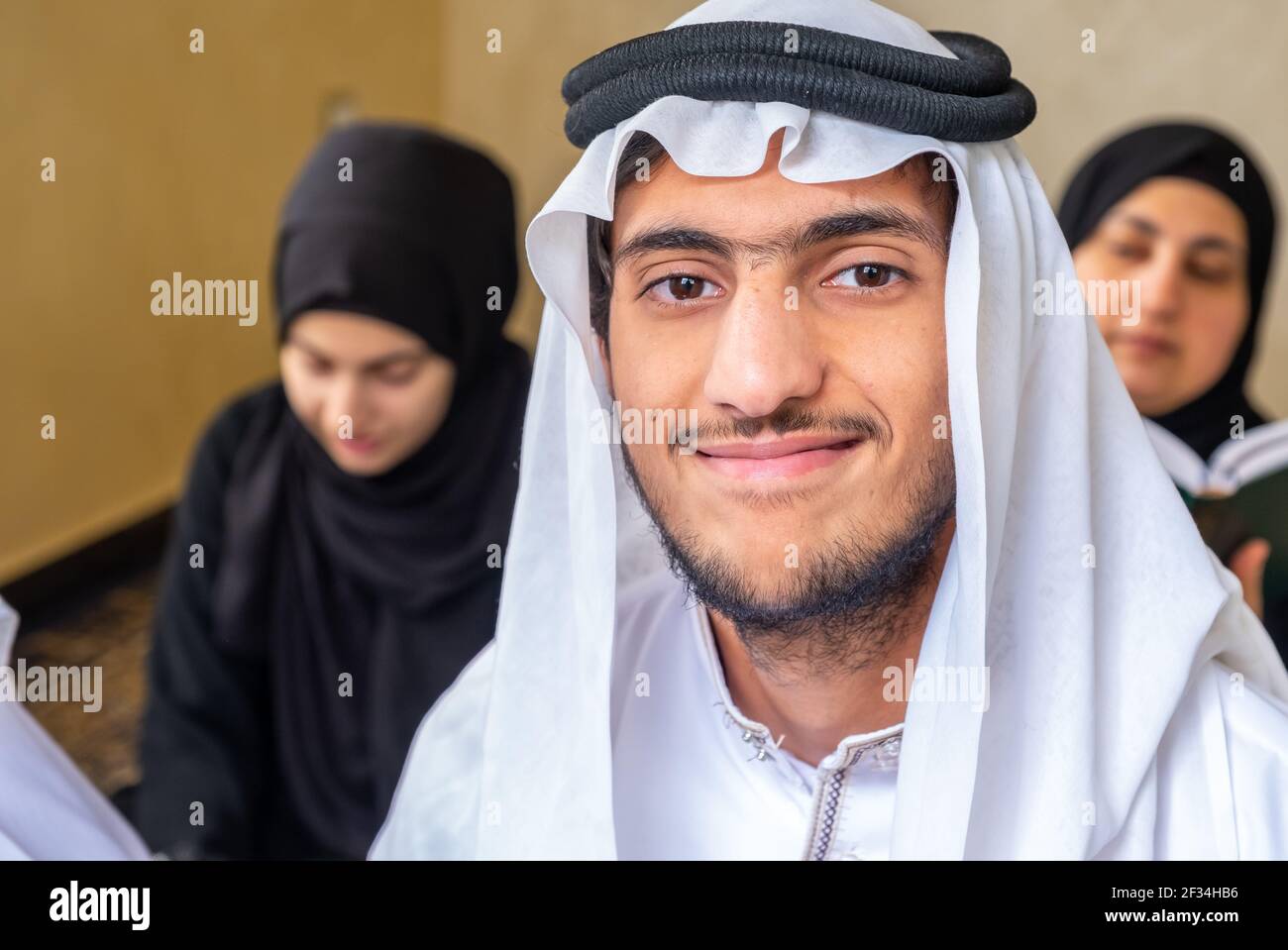 Muslim guy wearing Arabic clothes sitting with his family reading Quran ...