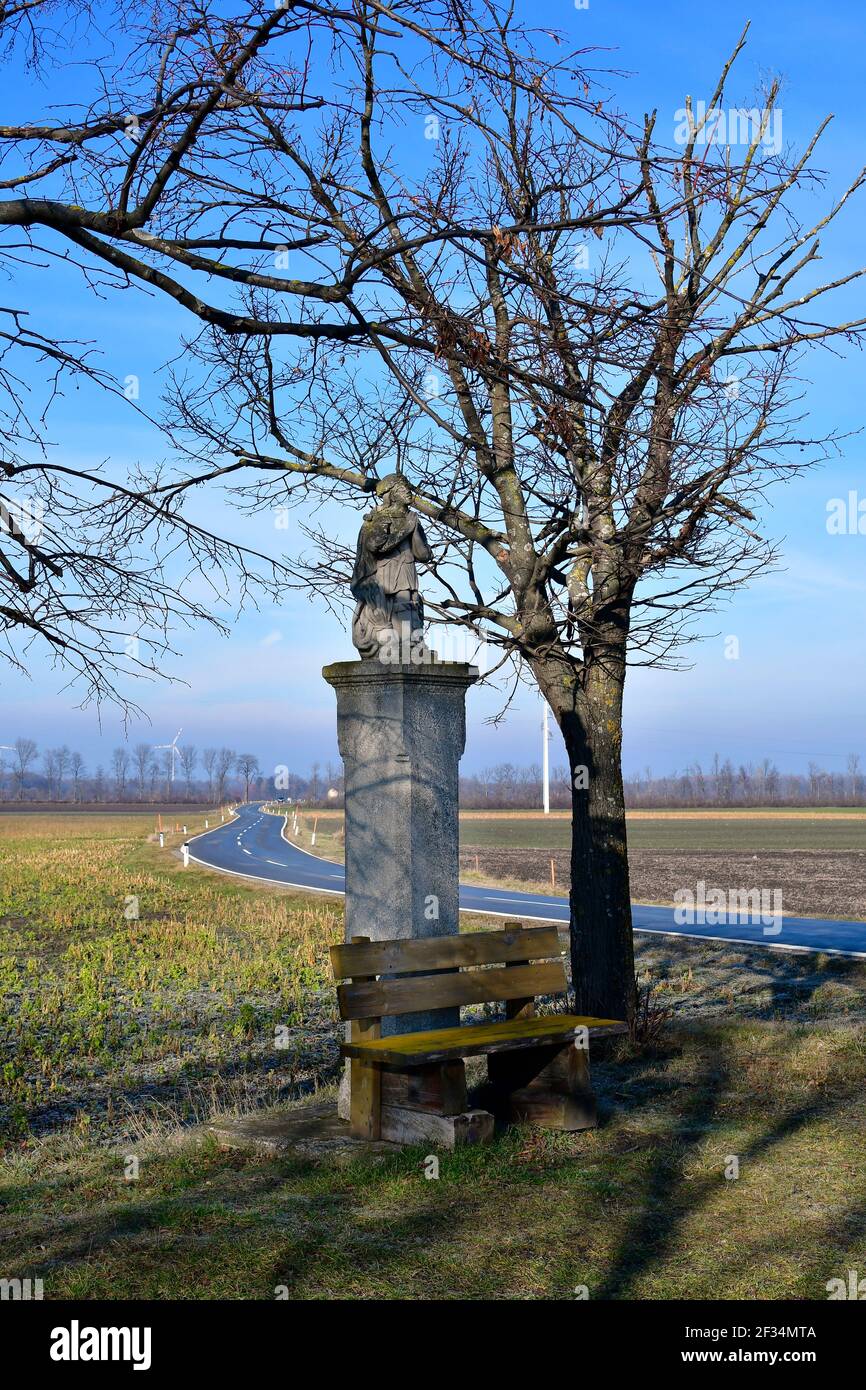 Austria, rest area on road with bench and statue of saint from 17th ...