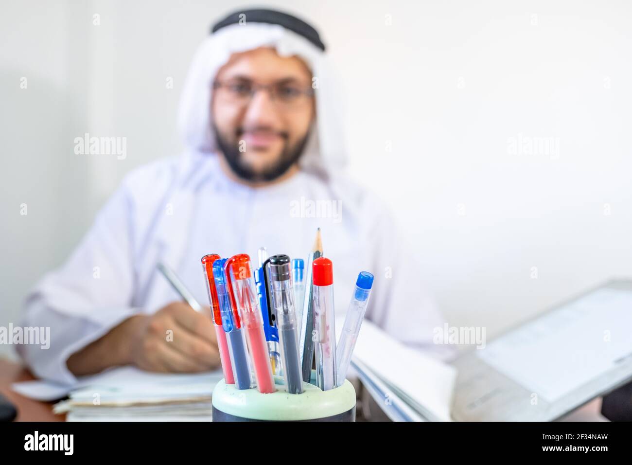 Happy Arabic Muslim man at work with a cup of pens in front of him ...
