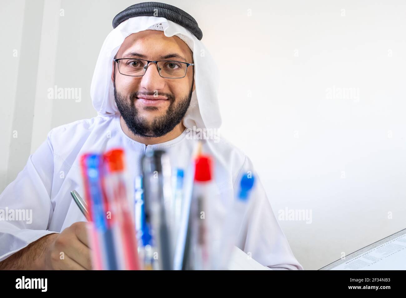 Happy Arabic Muslim man at work with a cup of pens in front of him ...