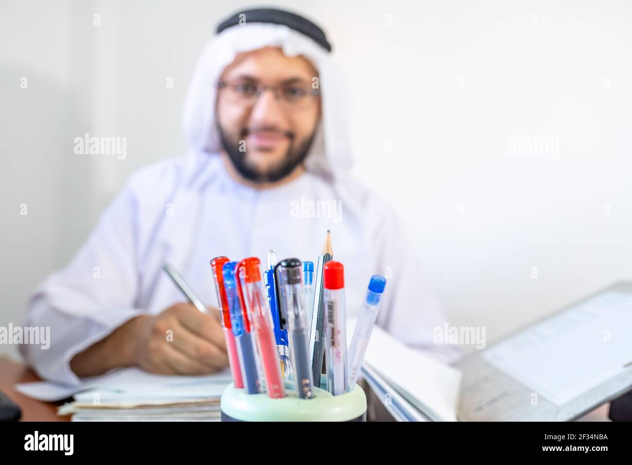 Happy Arabic Muslim man at work with a cup of pens in front of him ...