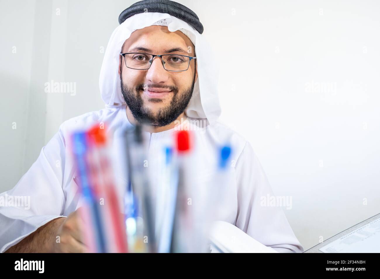 Happy Arabic Muslim man at work with a cup of pens in front of him ...