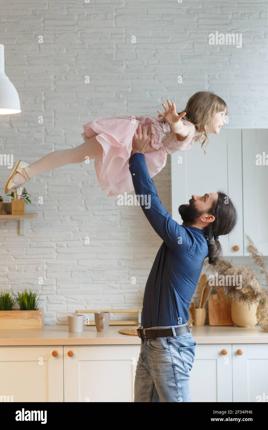 Happy young man lifting small preschool child daughter in air standing ...