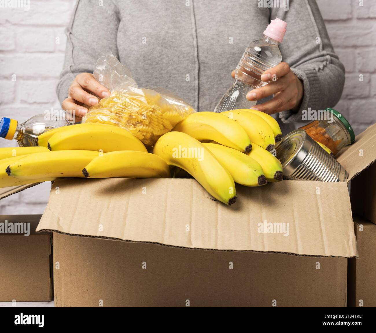 woman in a gray sweater puts in a cardboard box various foods, fruits ...