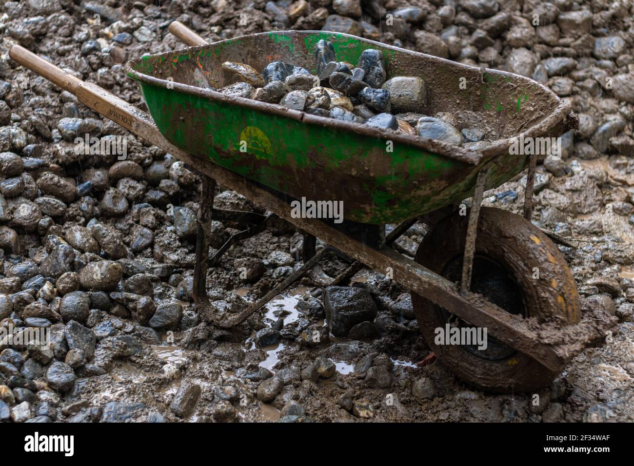 An old green wheelbarrow filled with stones in a muddy area Stock Photo ...