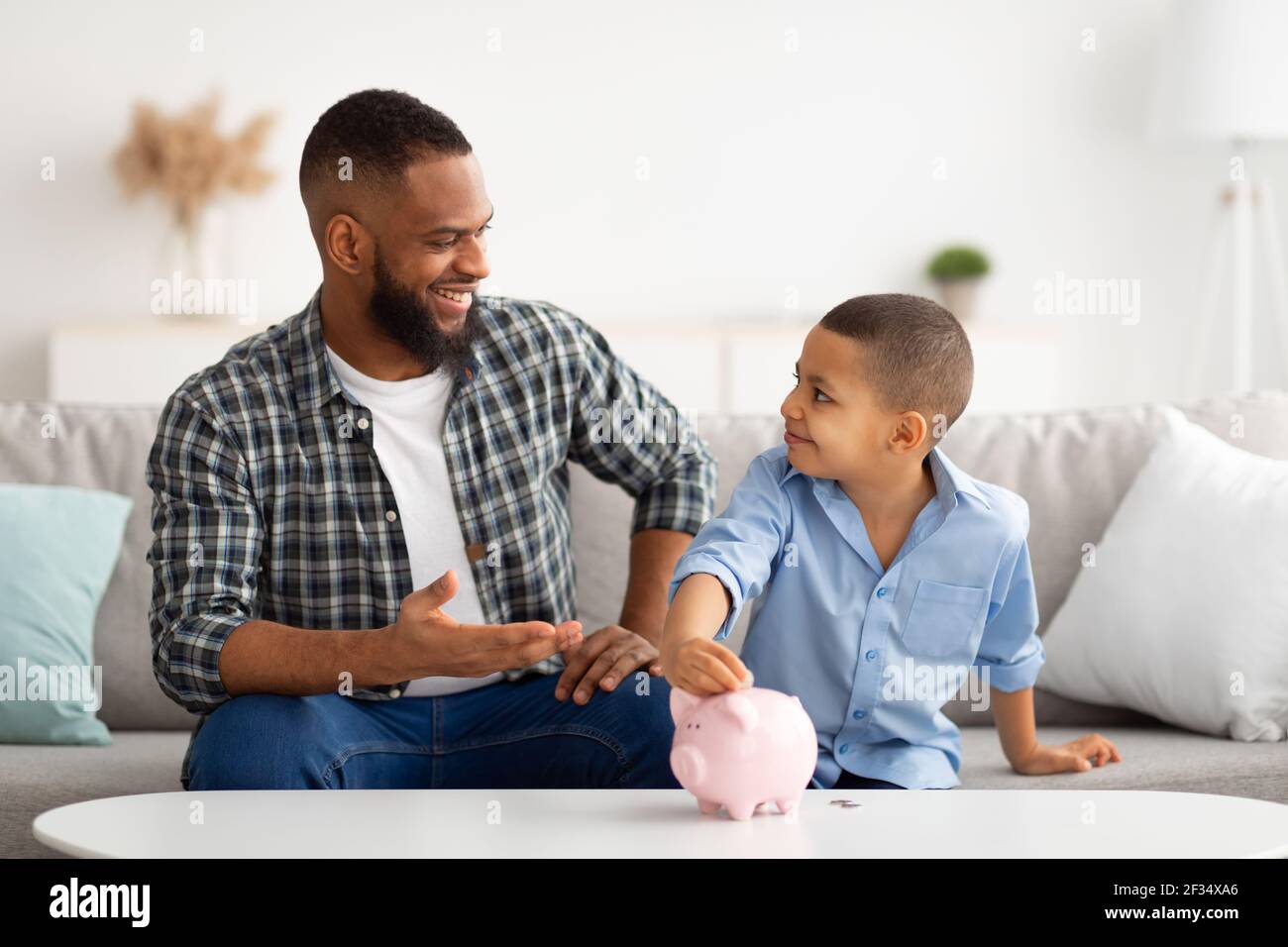 Father And Son Putting Personal Savings Money In Piggybank Indoor Stock ...