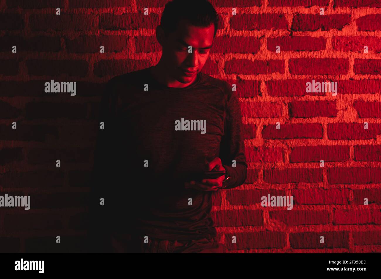 A Hispanic male with a smartphone on a brick wall background with red ...
