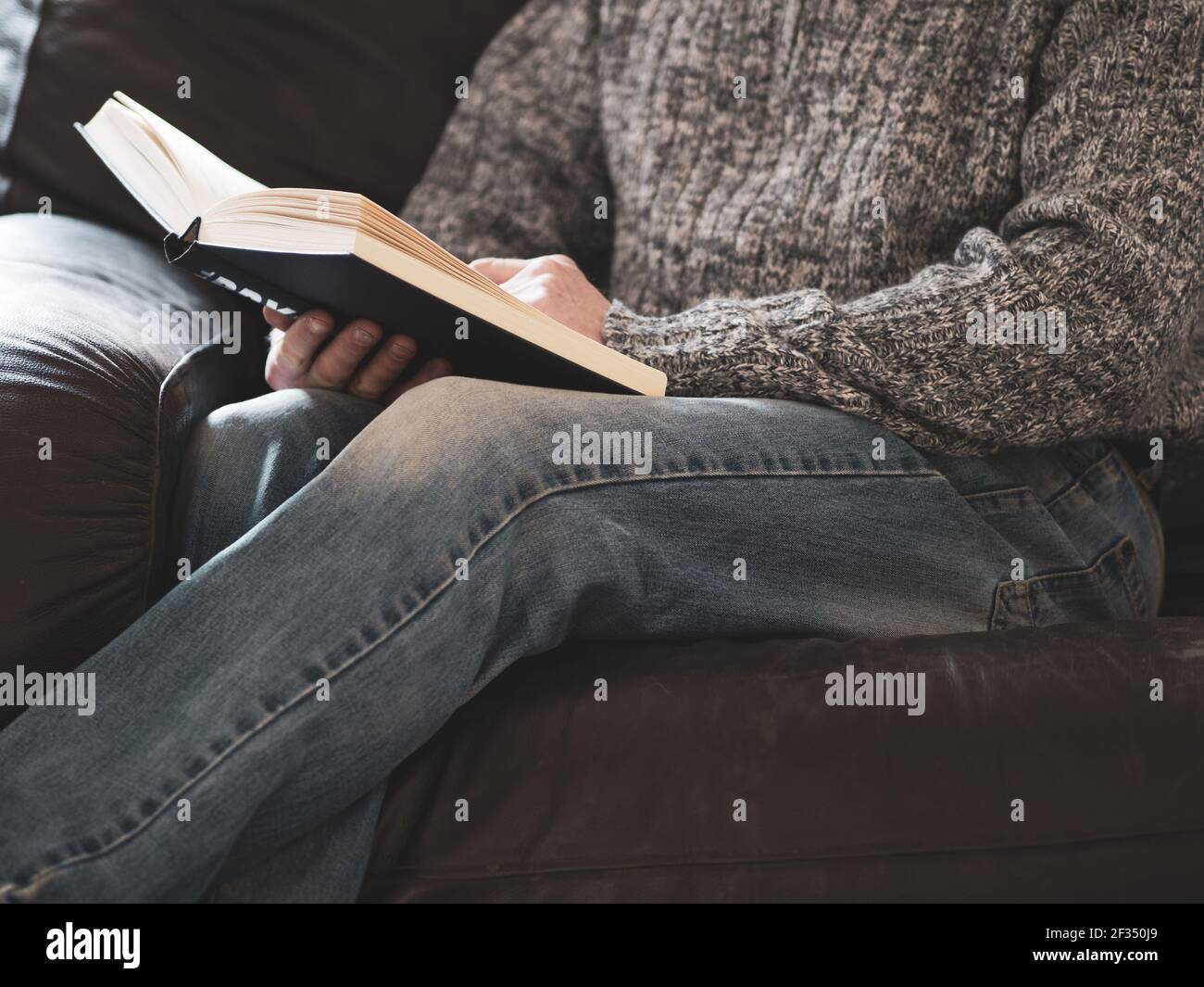 relaxing on chair reading a book casually dressed in blue jeans and ...