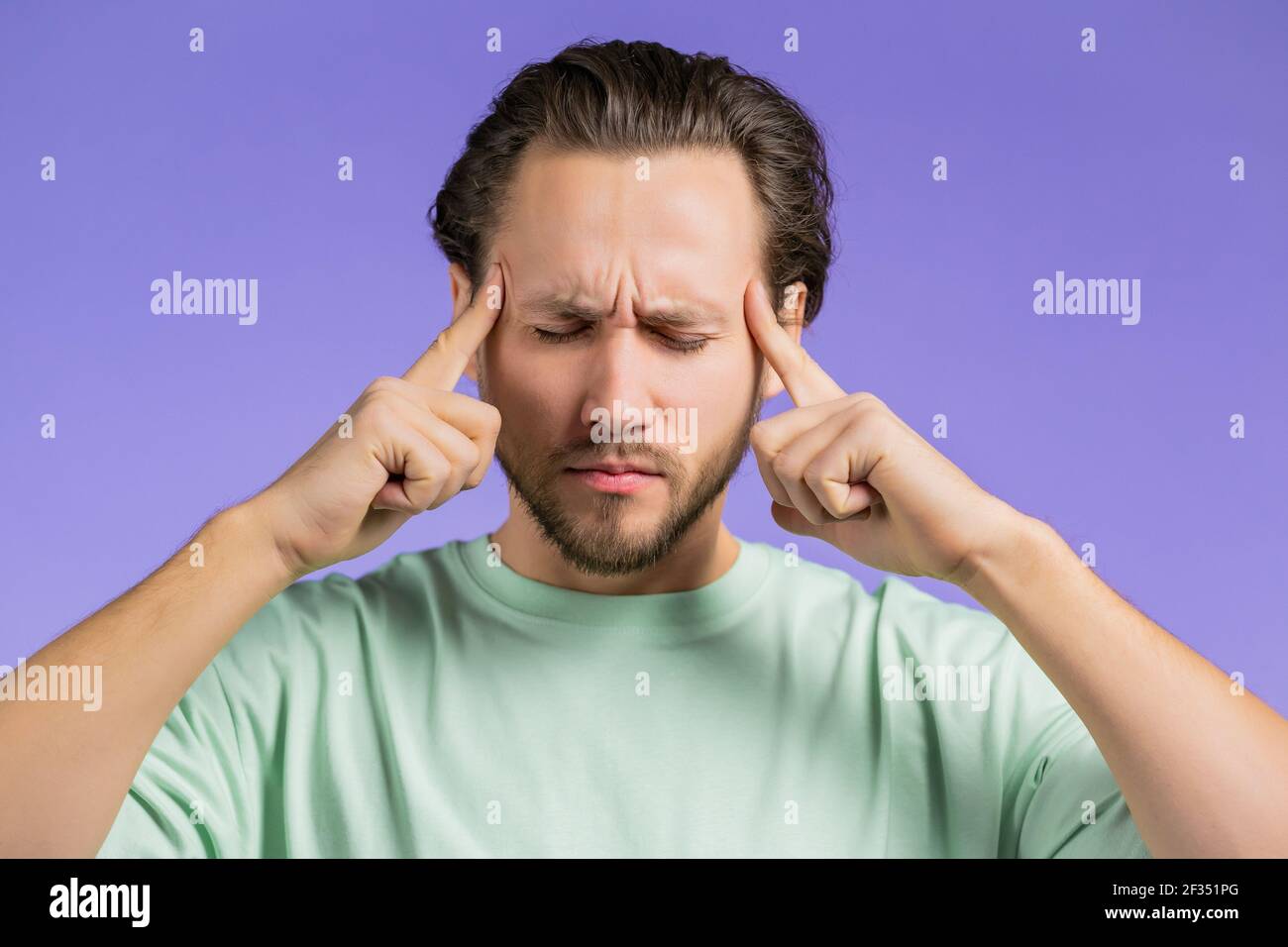 Young man having headache, studio portrait. Guy putting hands on head ...