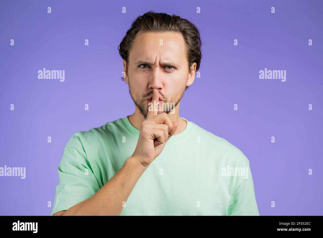 Serious man holding finger on lips over violet background. Gesture of ...