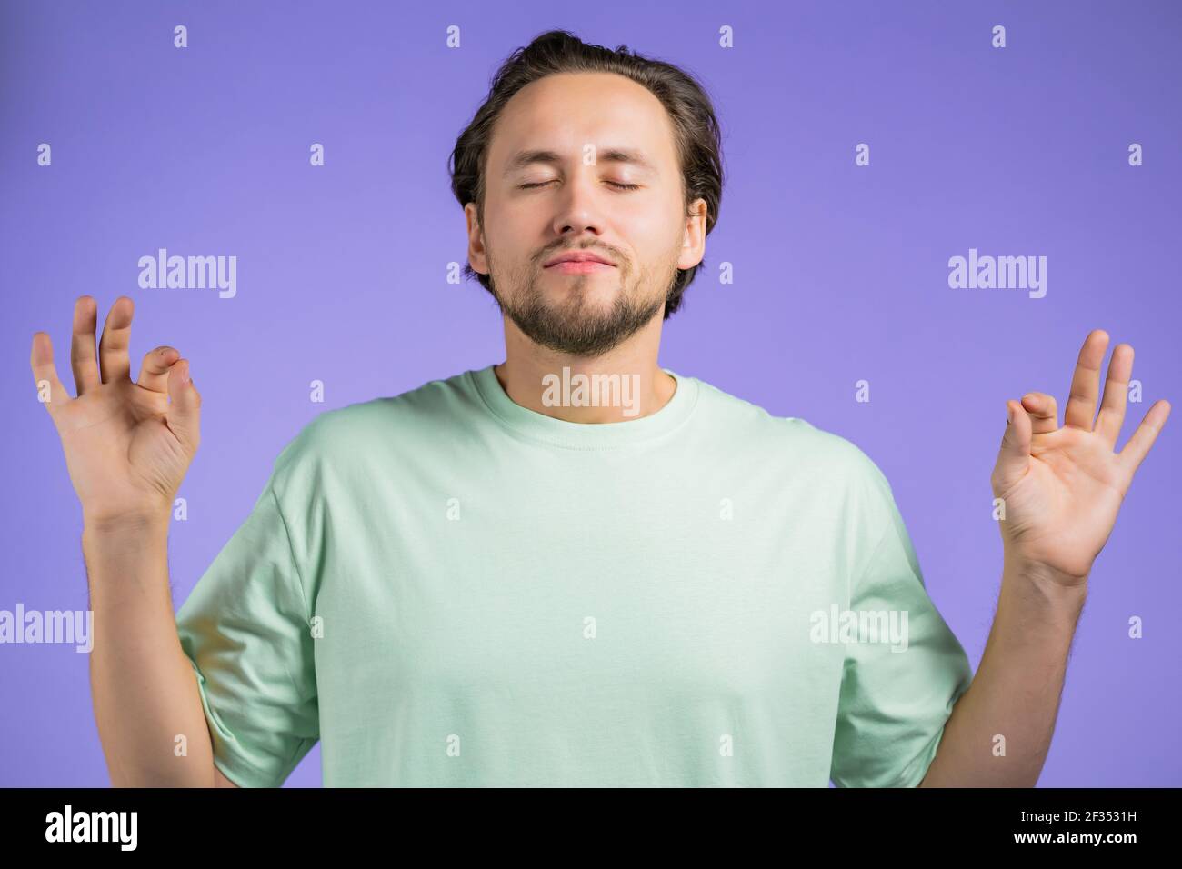 Calm man in basic t-shirt relaxing, meditating. He calms down, breathes ...