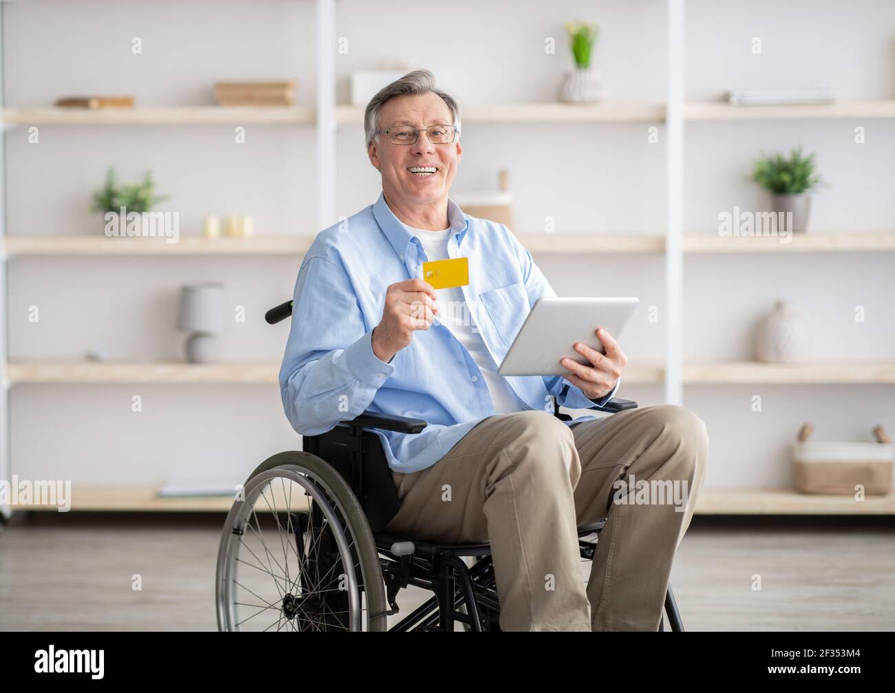 Happy disabled elderly man in wheelchair shopping online with tablet ...